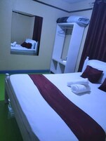 Quarto de hotel com uma cama de solteiro, um espelho, um guarda-roupa e um tapete verde.