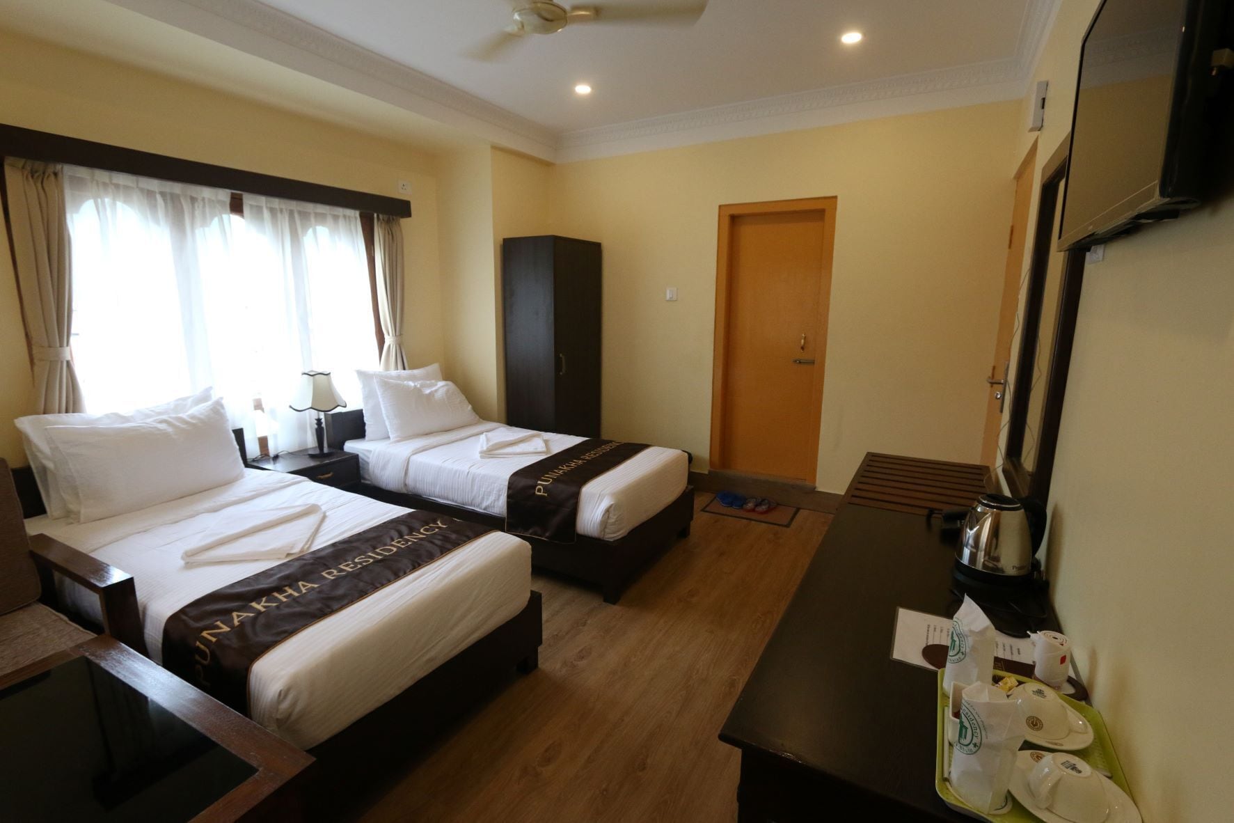 Quarto de hotel com duas camas, uma escrivaninha, televisão e um guarda-roupa.