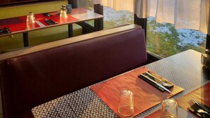 Um restaurante com área de assentos em cabines, uma mesa com jogo americano vermelho e vista para uma paisagem nevada através de cortinas translúcidas.