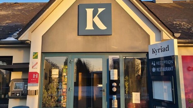 Um edifício com um logotipo 'K' bem visível, uma área de recepção e uma placa indicando um restaurante.