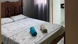 Quarto com cama, cabeceira de madeira, janela com cortinas e porta.
