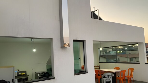 Um edifício moderno com grandes janelas, uma pequena varanda e uma área de refeições com cadeiras laranjas.