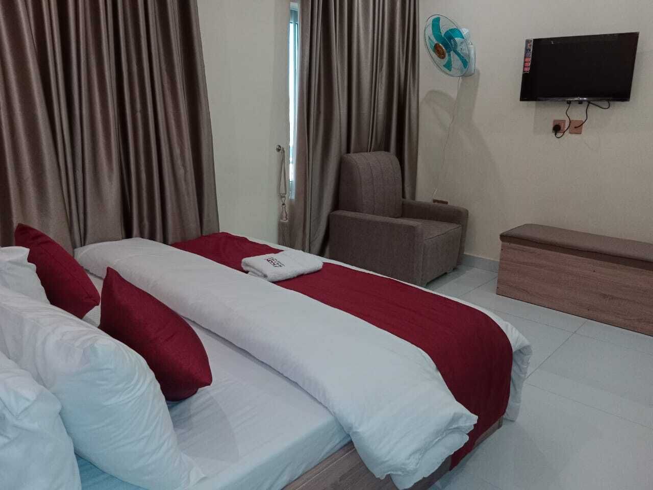 Quarto de hotel com cama, uma cadeira, uma televisão e um banco de madeira.