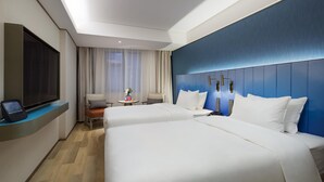 Quarto de hotel com duas camas, uma escrivaninha com televisão, uma mesinha de centro com um vaso e uma cadeira.