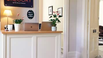 Balcão de recepção com dois laptops, placa indicando acomodações para hóspedes e placa de boas-vindas para Gregory pela The Warren Collection.