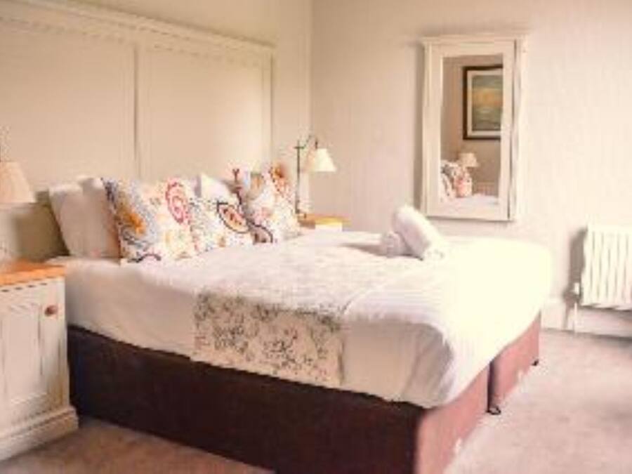 Quarto com cama, mesa de cabeceira, abajur e radiador.