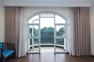 Um quarto com uma grande janela em arco, uma cadeira de madeira e uma varanda com grades de metal.