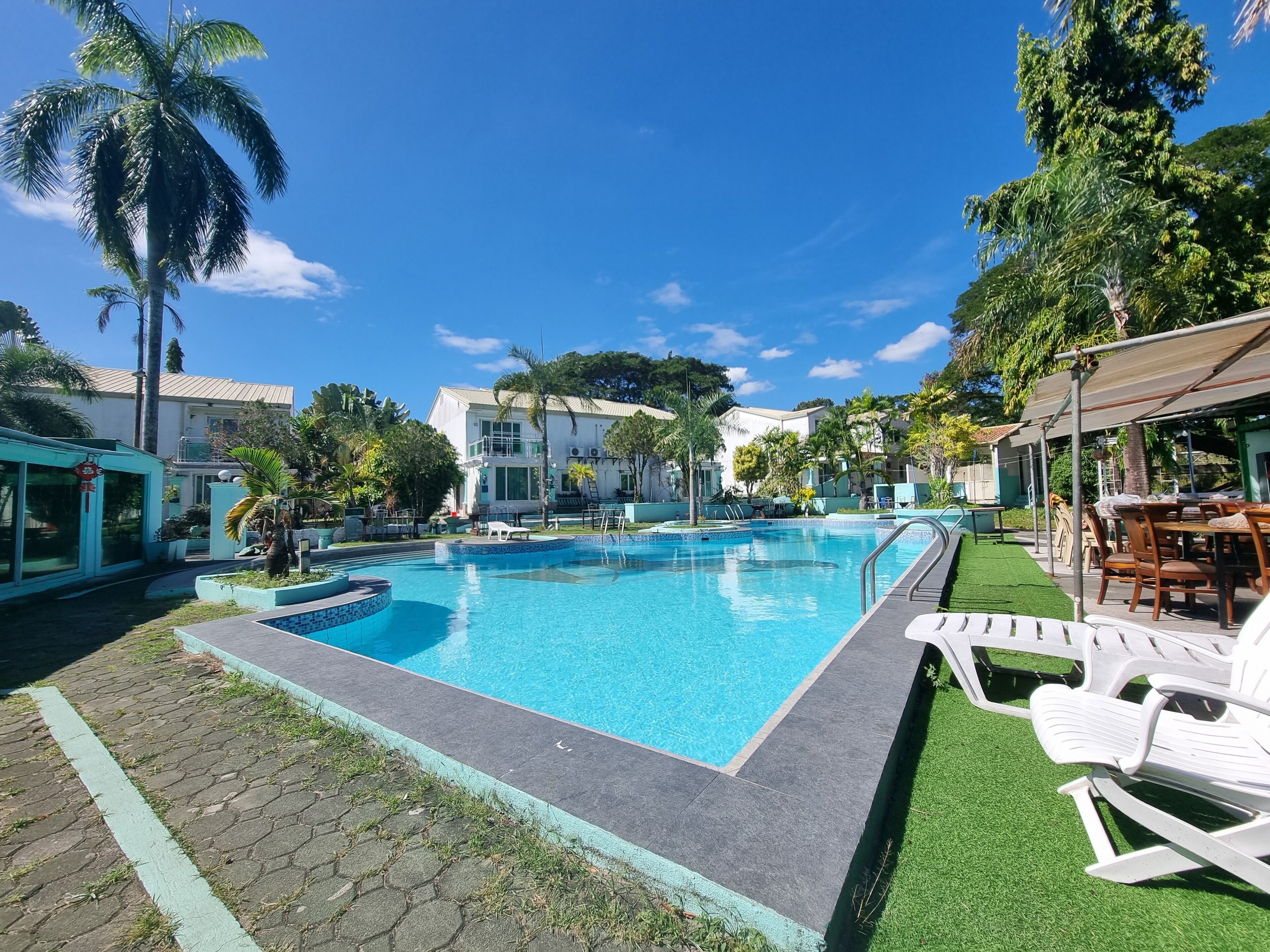 Piscina com borda azulejada, rodeada por espreguiçadeiras e um gramado.