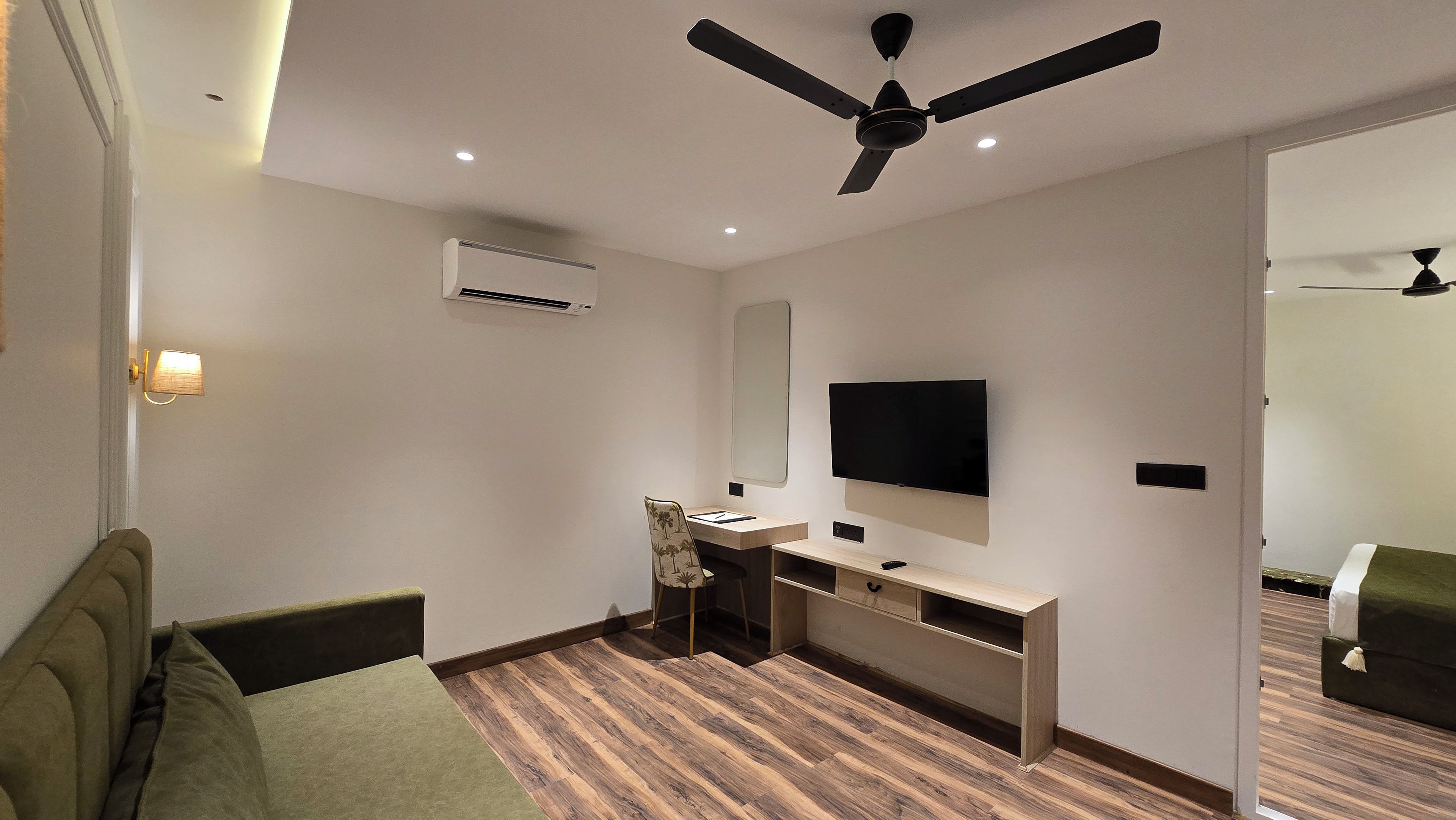 Quarto de hotel com cama, escrivaninha, cadeira, televisão de tela plana, ar condicionado e ventilador de teto.
