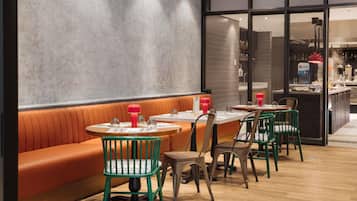 Interior de restaurante moderno com um longo banco laranja, mesas redondas e cadeiras verdes.