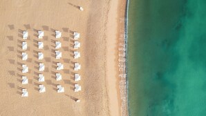 Vista aérea de uma praia com fileiras de guarda-sóis brancos e cadeiras de praia dispostas em um padrão de grade.