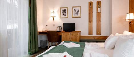 Quarto de hotel com uma cama, uma escrivaninha, uma televisão e duas molduras na parede.