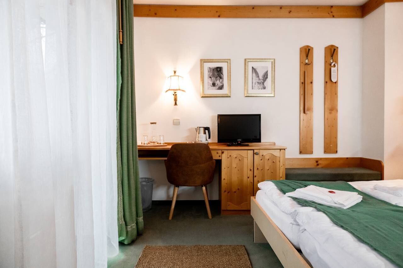 Quarto de hotel com cama, escrivaninha com computador, cadeira, abajur e duas quadros na parede.