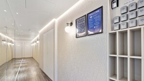 Corredor moderno de hotel com piso de madeira, paredes de vidro e placa de boas-vindas.