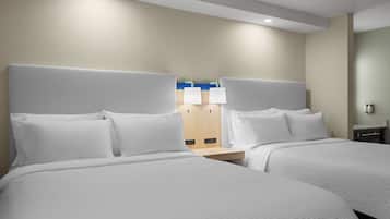 Quarto de hotel com duas camas, um guarda-roupa de madeira e uma mesa de cabeceira com abajur.