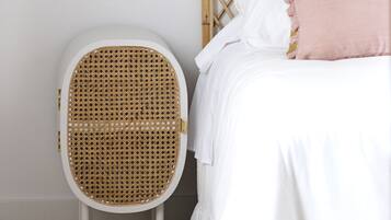 Quarto com cama, cadeira de vime e um objeto decorativo na parede.