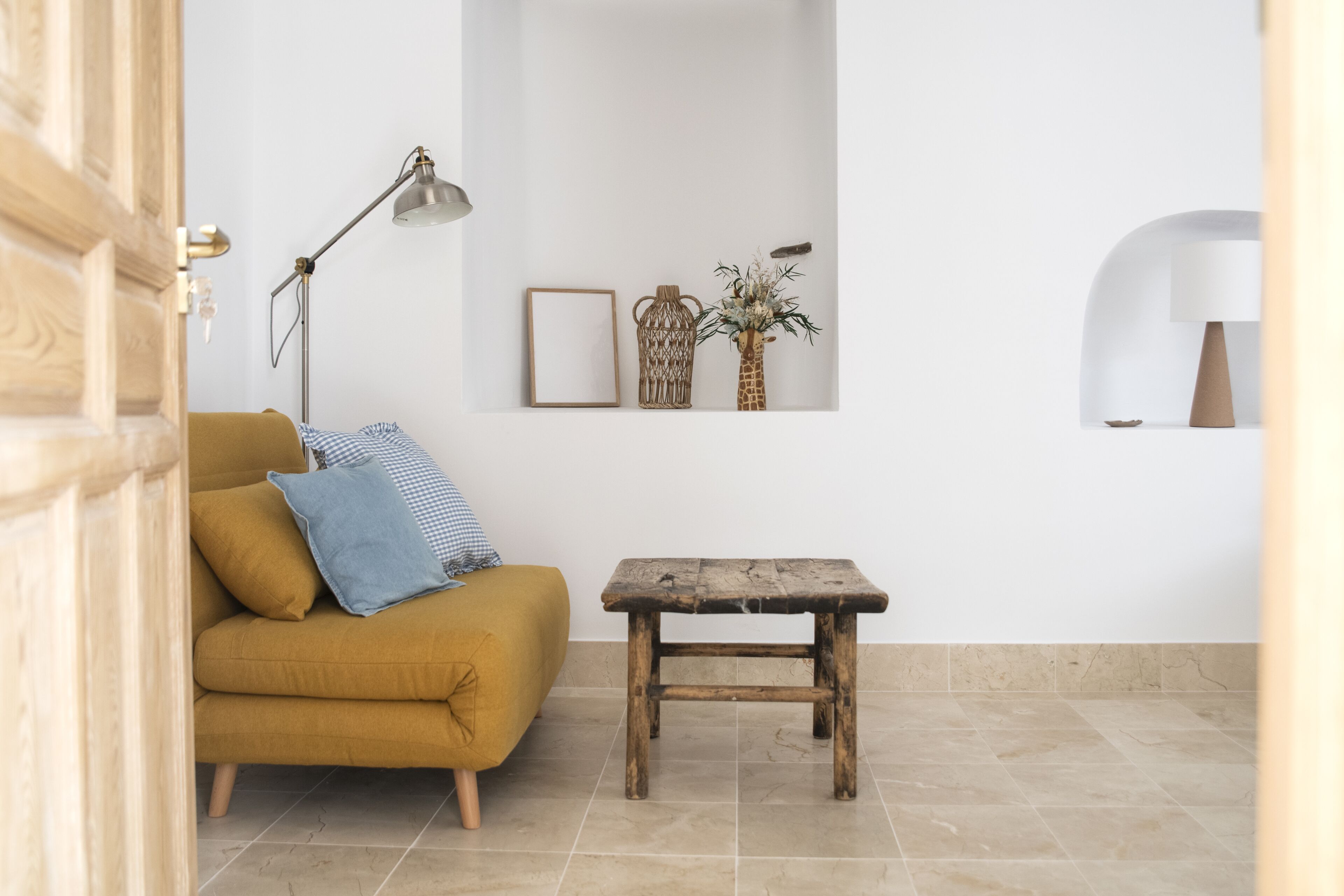 Quarto com sofá cor mostarda, uma pequena mesa de madeira, luminária de chão e decoração na parede.