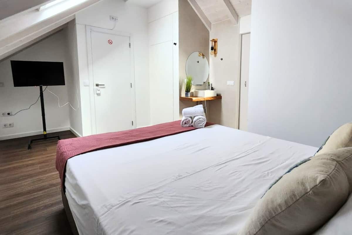 Quarto de hotel com uma cama, televisão, escrivaninha com espelho e uma parede com detalhes em vermelho.