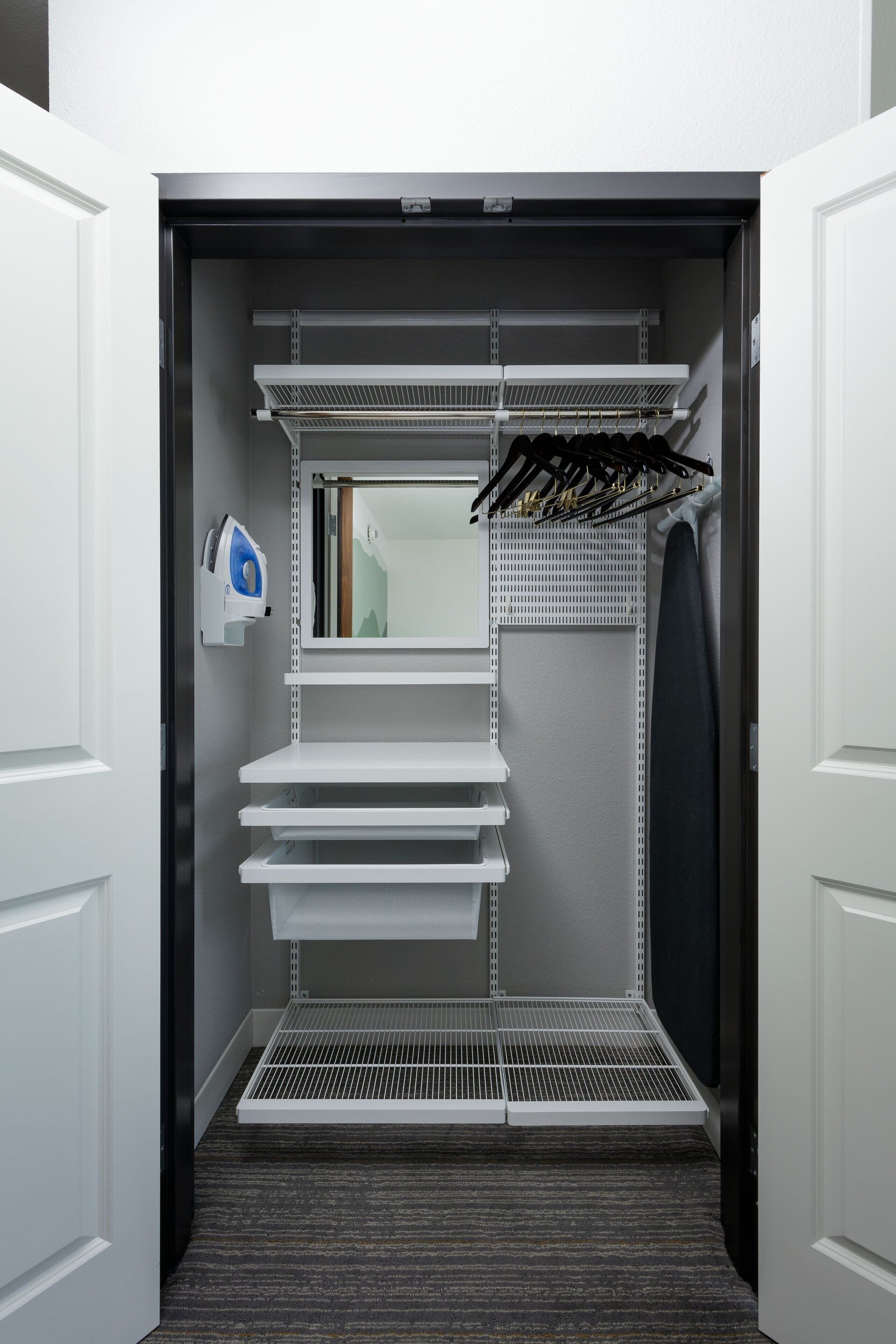 Um closet amplo com prateleiras, cabideiro e um espaço para passar roupa embutido.