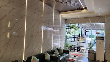 Um hall moderno com parede de mármore, sofá de couro preto e porta de vidro que dá para o exterior.