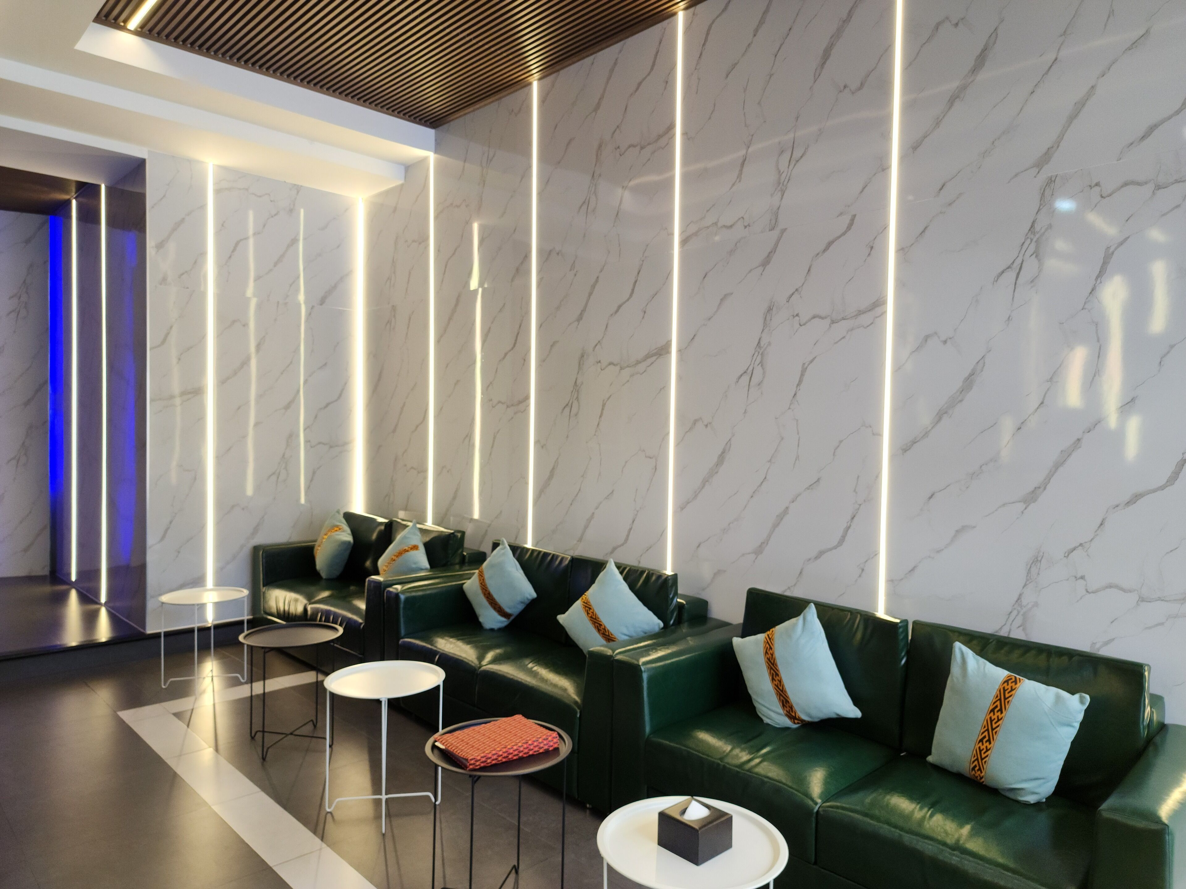 Um hall moderno com um conjunto de sofá verde, paredes de mármore branco e um design de teto elegante.