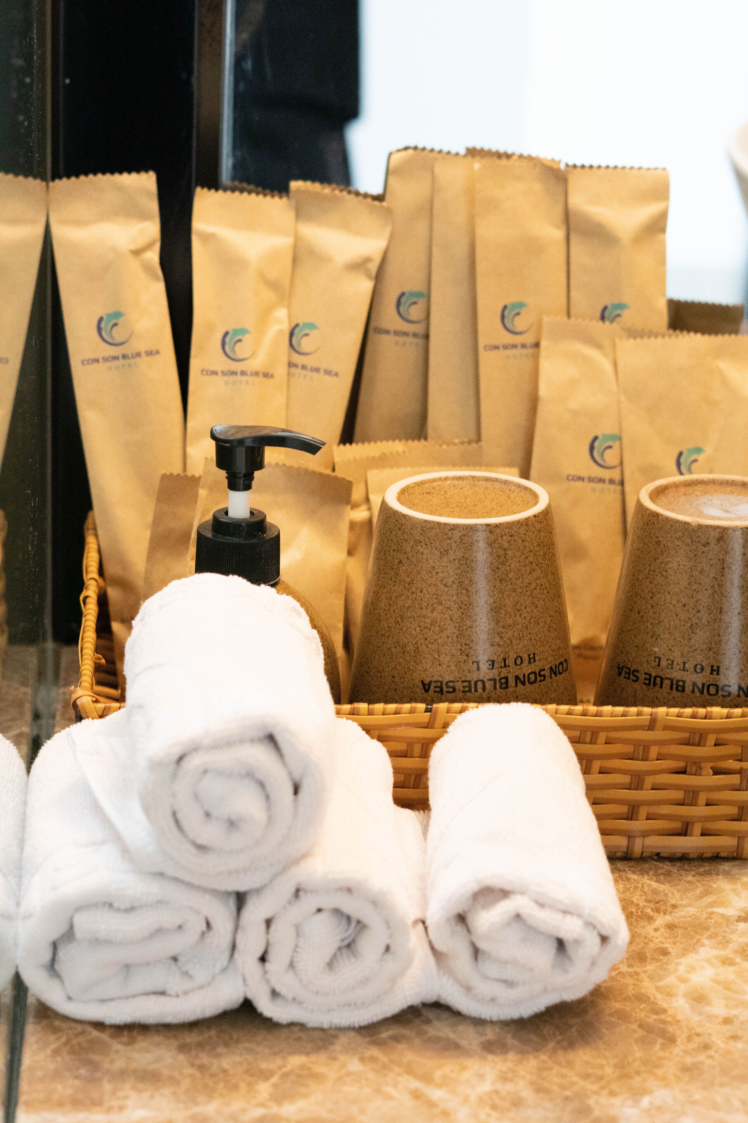 Casa de banho com divisória de vidro, cesto de vime com toalhas dobradas e vários sacos de papel castanho com um logótipo.