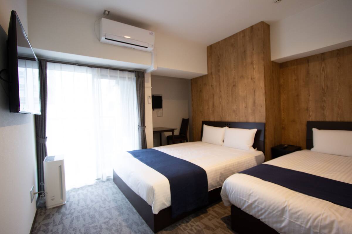 Quarto de hotel com duas camas, televisão, ar condicionado e janela com cortinas.