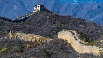 Um muro de pedra histórico com uma torre de vigia numa colina, rodeado por terreno montanhoso.