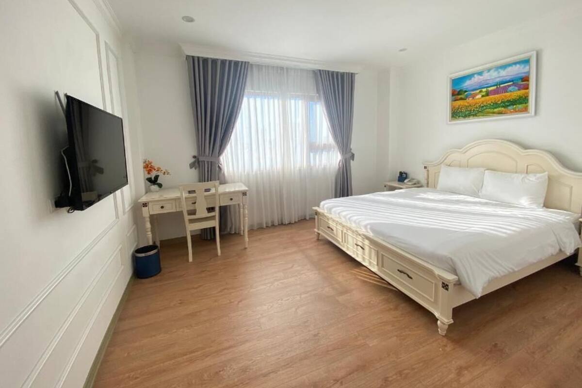 Quarto com cama, escrivaninha, cadeira, televisão e um quadro na parede.