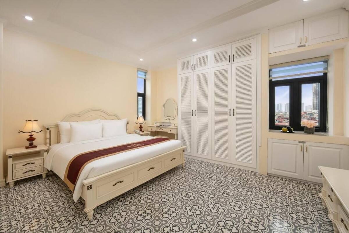 Quarto com cama, mesas de cabeceira, guarda-roupa e janela com vista para a cidade.