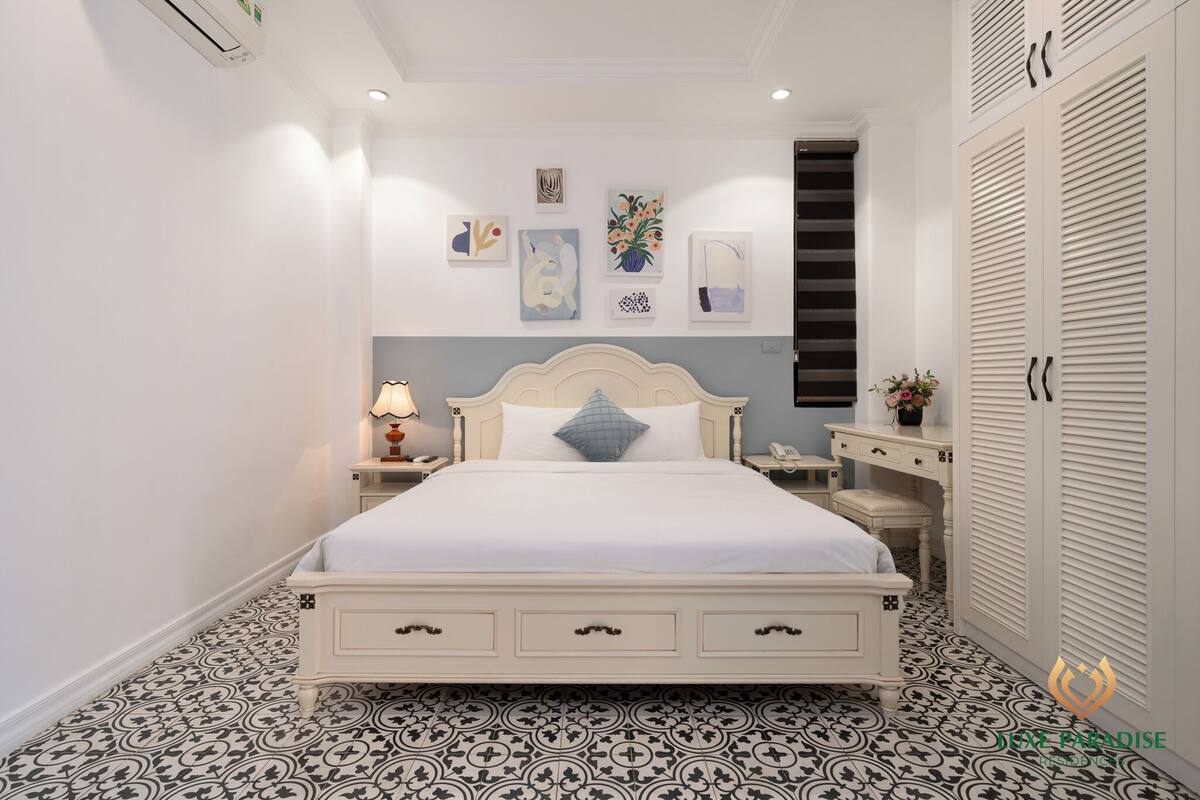 Um quarto bem organizado com uma cama, mesas de cabeceira, um guarda-roupa e uma parede decorada com obras de arte.