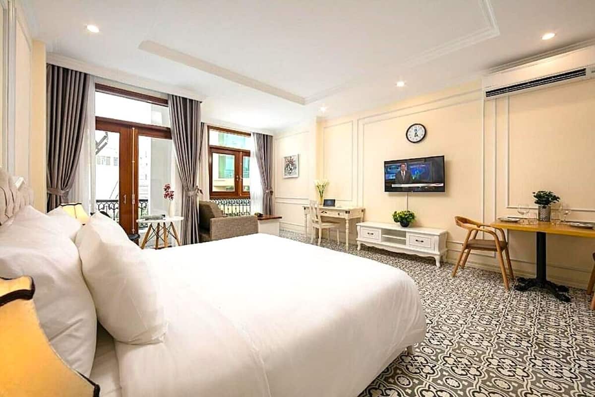 Quarto de hotel com uma cama grande, escrivaninha, televisão e janela com cortinas.