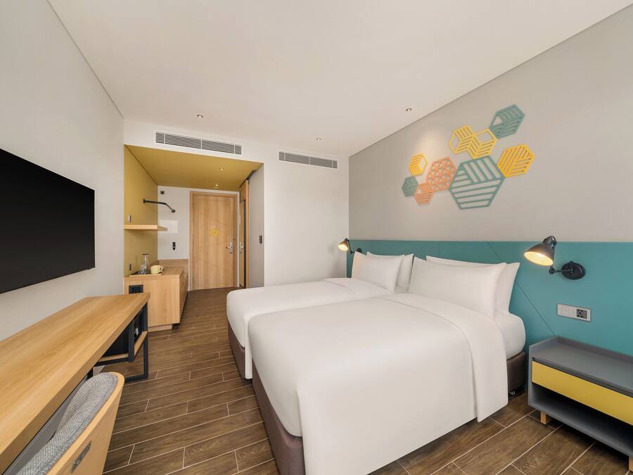 Quarto de hotel moderno com uma cama grande, uma escrivaninha, uma TV e um banheiro visível através de uma porta aberta.