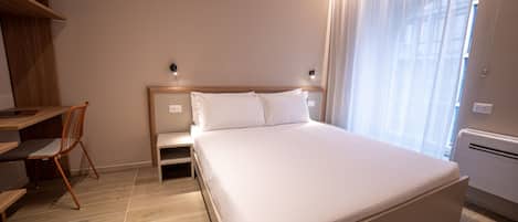 Quarto com cama, escrivaninha, cadeira e janela com cortinas.
