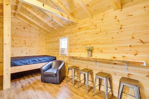 Quarto de cabana de madeira com beliche, poltrona de couro e três banquetas de metal.