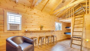 Interior de uma cabana de madeira com sofá, banquetas, escada e beliche.