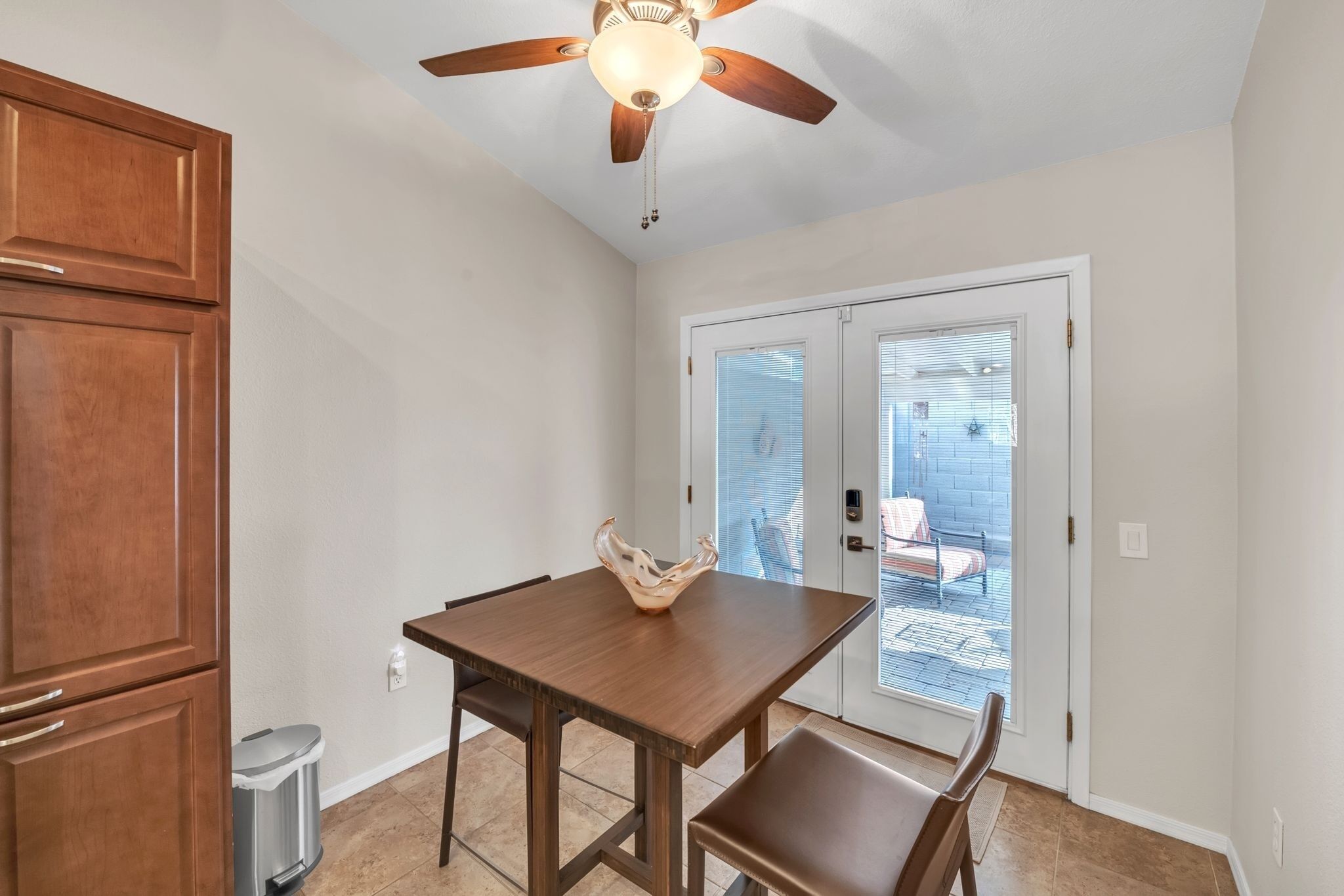 Uma área de jantar com mesa e cadeiras de madeira, um ventilador de teto e vista para o pátio através de uma porta de vidro.