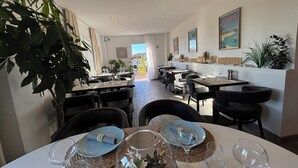 Restaurante com mesas preparadas para refeições, uma grande planta em vaso e obras de arte emolduradas nas paredes.