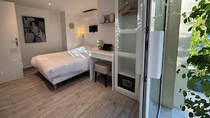 Quarto com cama, escrivaninha, guarda-roupa e porta que dá para uma varanda com vegetação.
