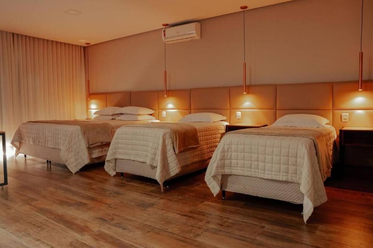 Quarto de hotel com três camas, cada uma com cabeceira e abajures.
