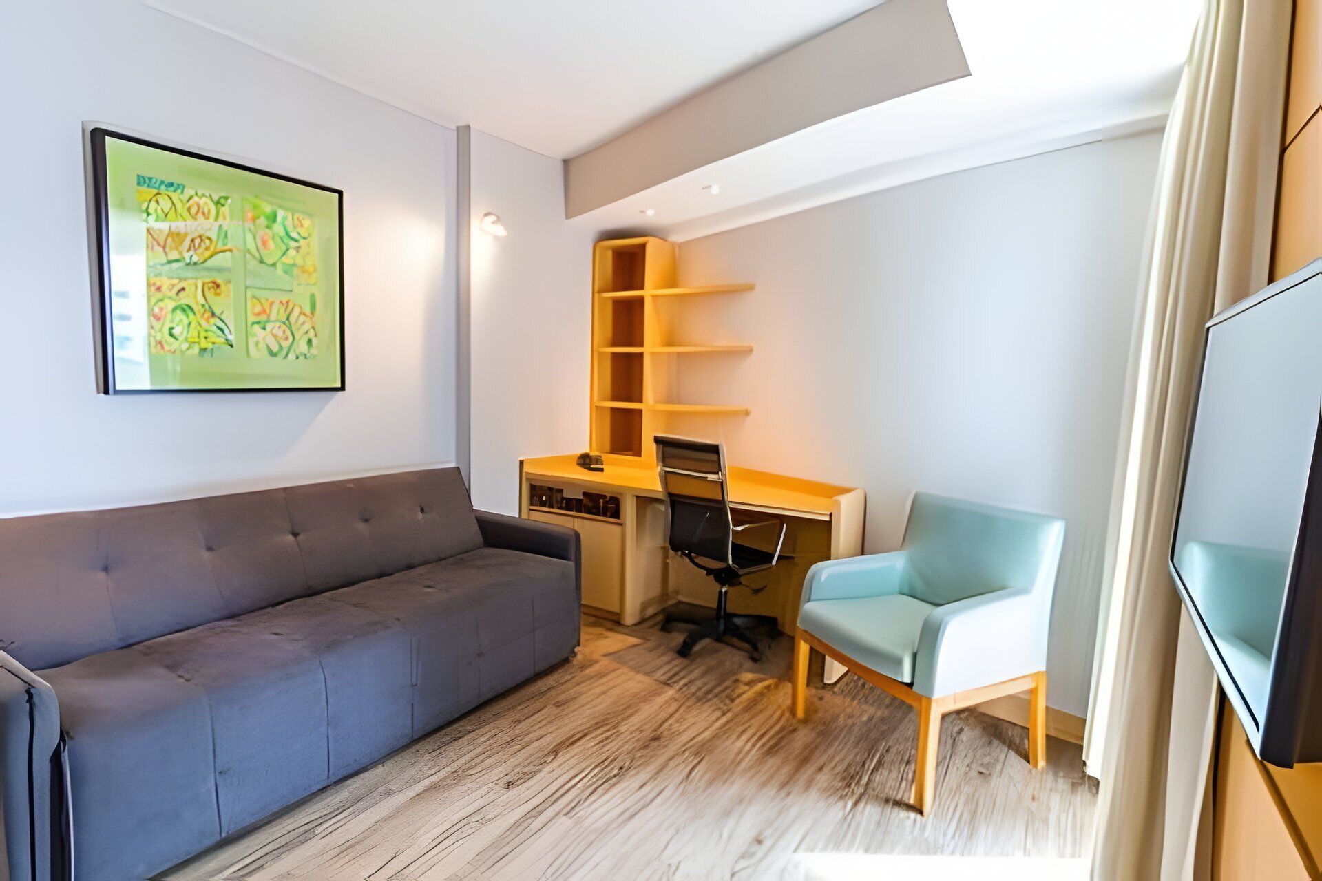 Quarto moderno com sofá cinzento, escrivaninha com cadeira, televisão e estante de livros.