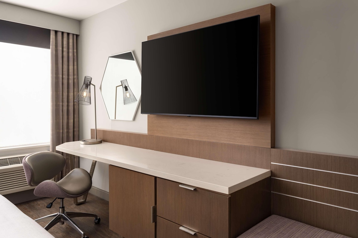 Quarto de hotel moderno com uma grande televisão de tela plana na parede, uma escrivaninha com cadeira e um espelho grande.