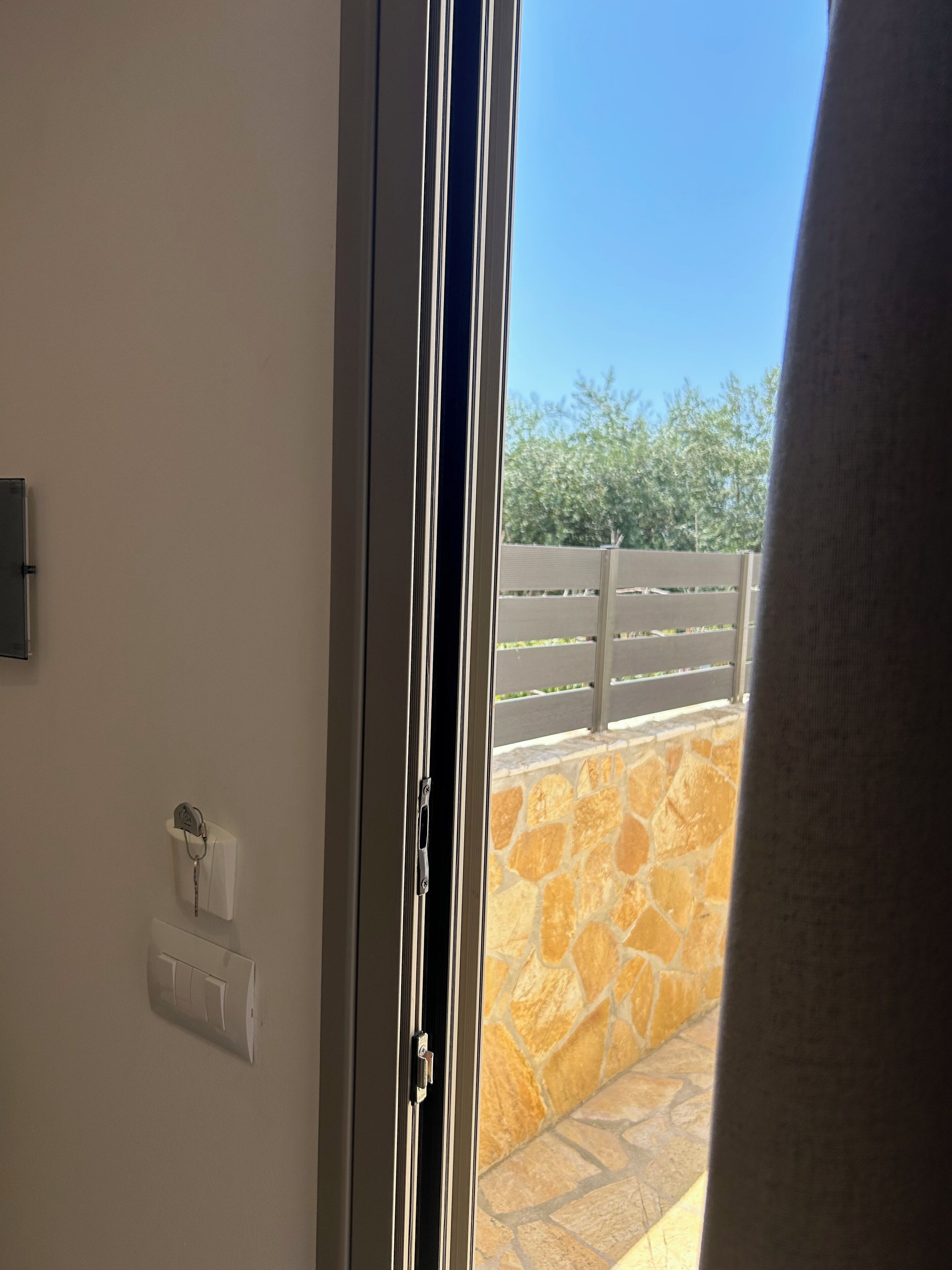 Visão através de uma porta, com uma parede de pedra e cerca de madeira no exterior.