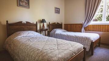 Quarto com duas camas de solteiro, cabeceiras de madeira, mesa de cabeceira com abajur e quadros nas paredes.