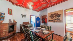 Uma sala de jantar com teto estampado em vermelho, lareira de tijolos e mesa tradicional posta para quatro pessoas.