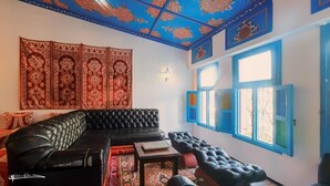 Um quarto com sofá de couro preto, tapeçaria estampada e janelas com moldura azul.