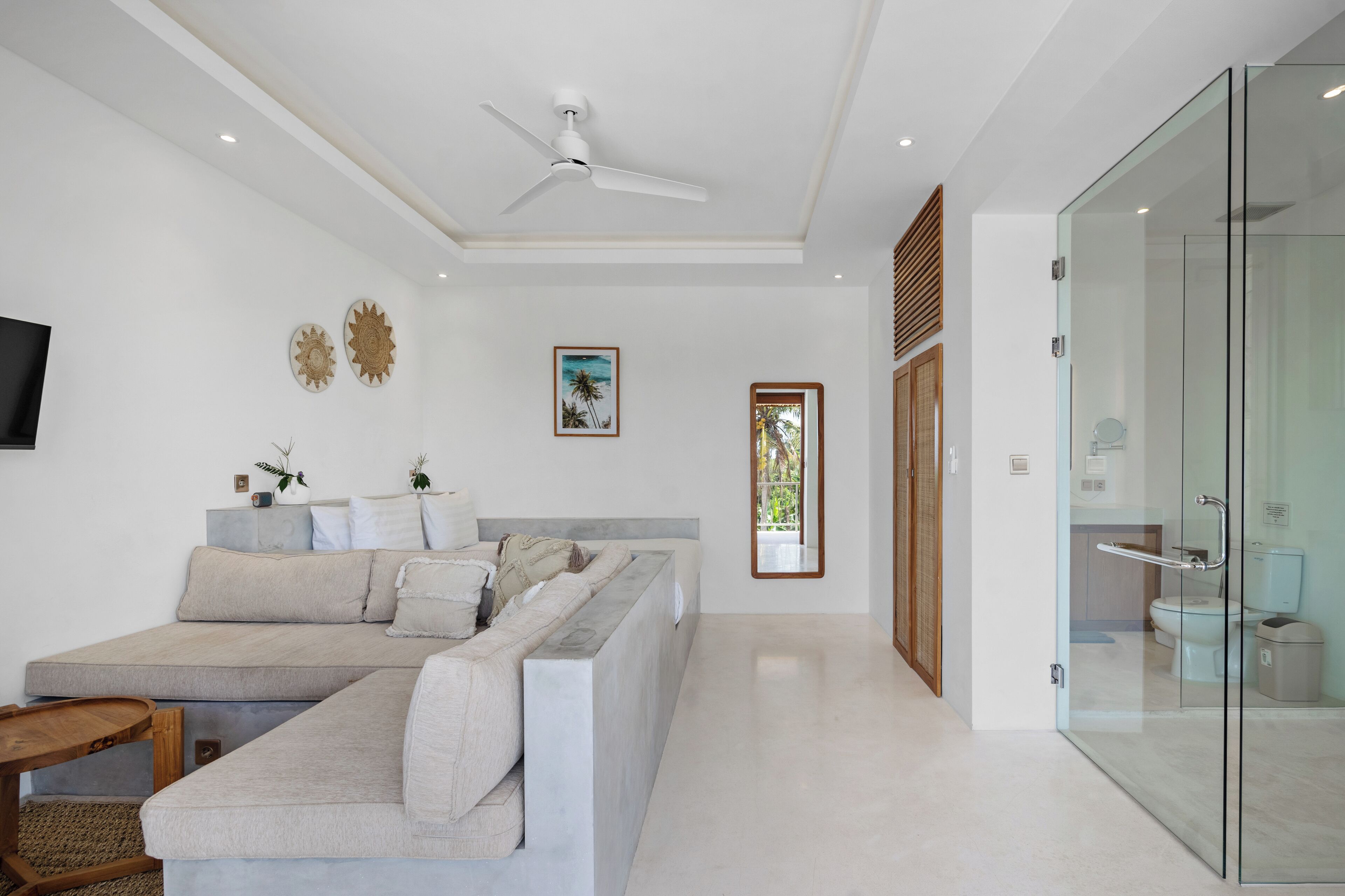 Uma sala moderna com um sofá seccional, um ventilador de teto e um box de vidro.