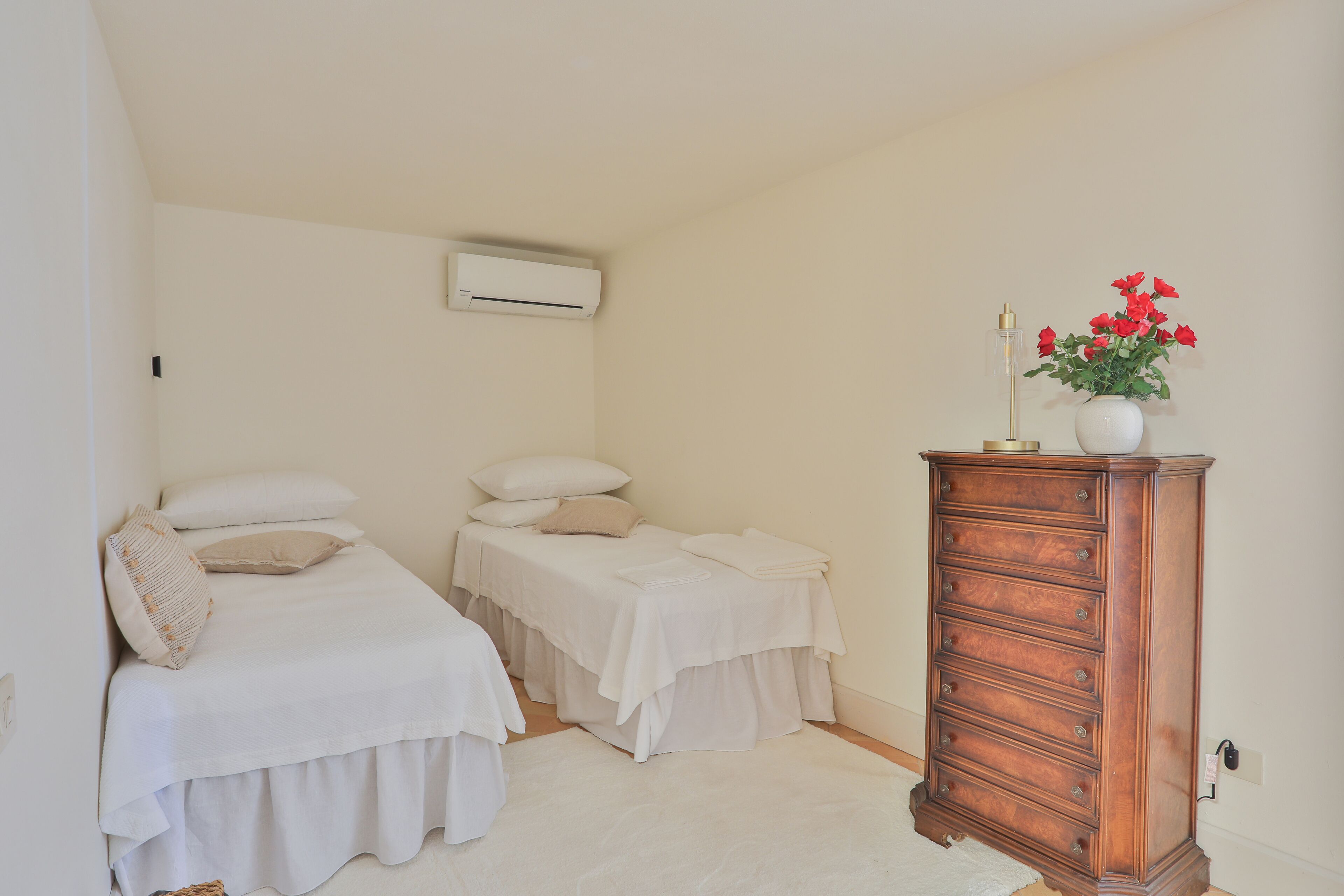 Quarto com duas camas de solteiro, cômoda e ar-condicionado fixado na parede.