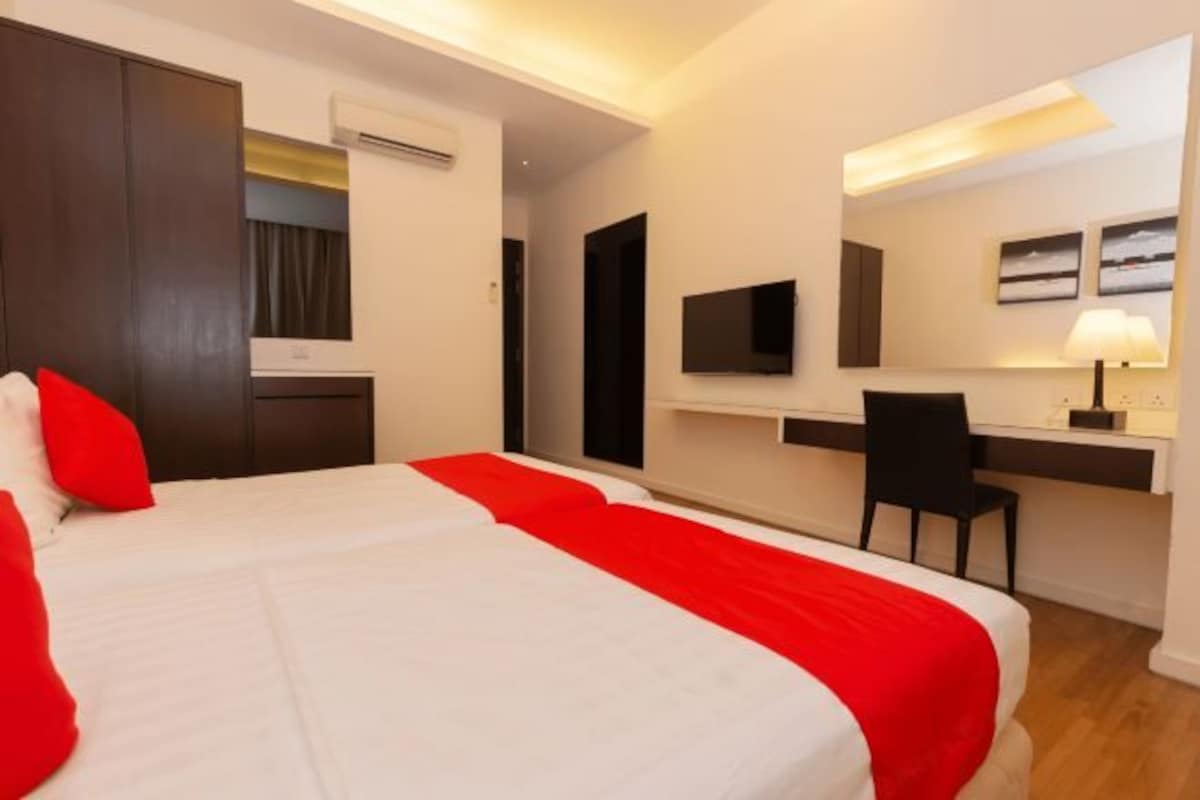 Quarto de hotel com cama, escrivaninha, cadeira, televisão e janela.