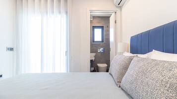 Quarto de hotel com uma cama grande, banheiro com pia e vaso sanitário, e janela com cortinas.
